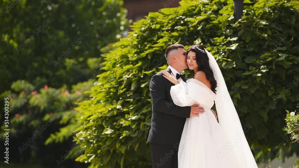 Bride and groom kiss at park in luxury mansion courtyard. Man in black ...