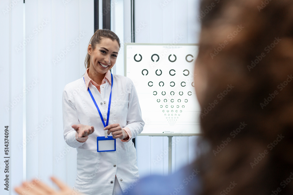Professional female optician pointing at eye chart, timely diagnosis of ...