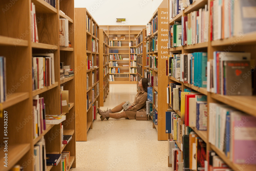 Young woman sitting at the library holding book. millennial reading ...