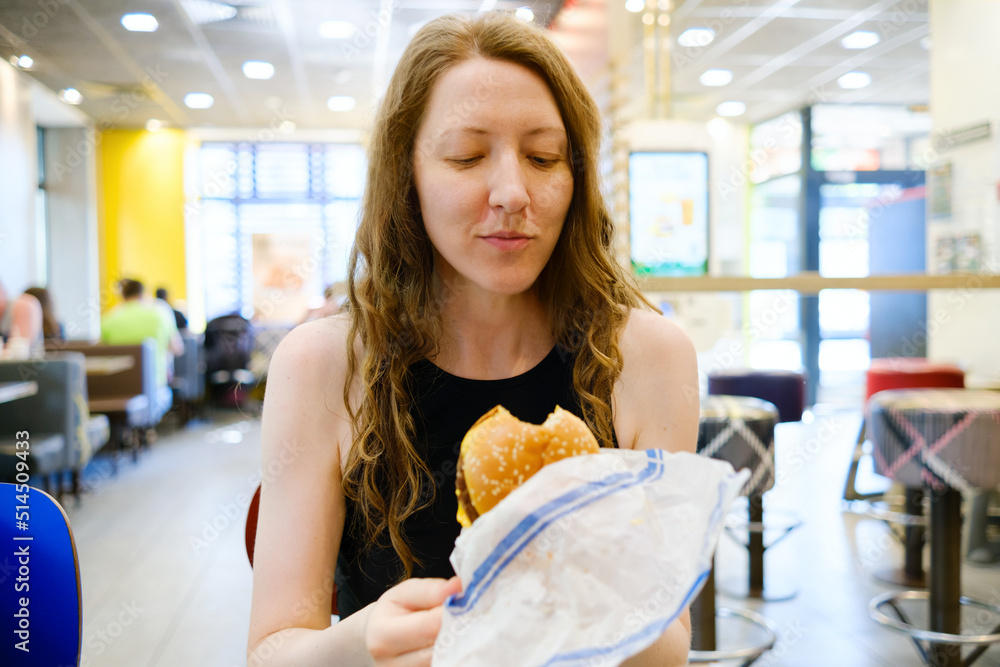 Woman with burger in a fast food restaurant. Woman opening wrapping ...