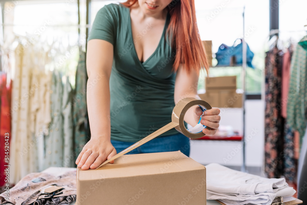 Cutaway view of a young businesswoman, packing a box with tape, for a ...