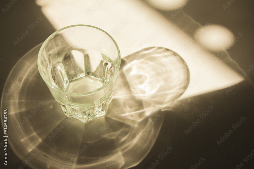 glass with sparkling sunlight shadow on the white background. Minimal ...