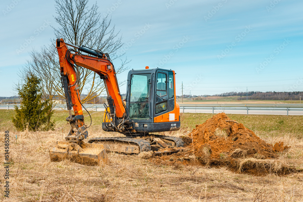 Mini excavator digging earth in a field or forest near roadway.Digging ...