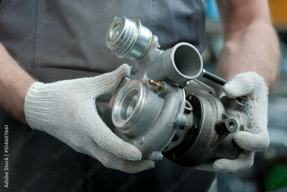 Car maintenance. An auto mechanic holds a new turbocharger in his hands ...