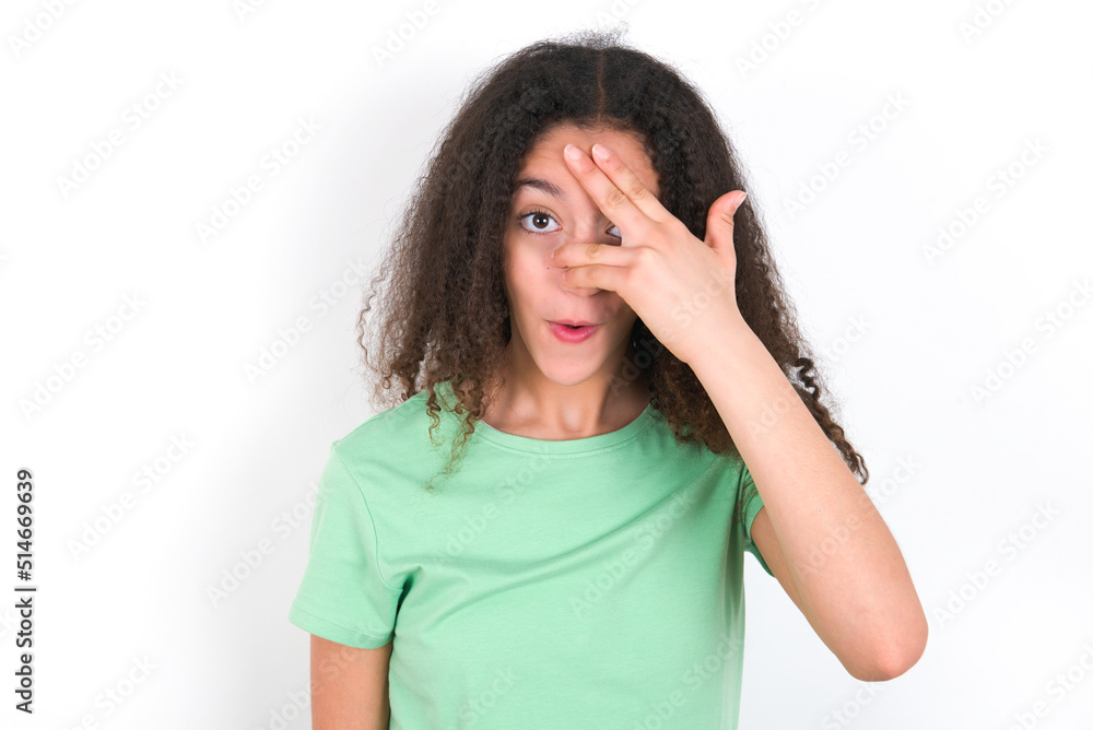 Teenager girl with afro hairstyle wearing green T-shirt over white wall ...