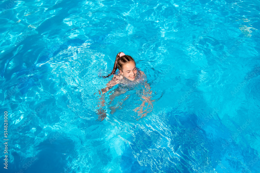 A teenage girl of 11-13 years old swims in a pool with blue water. She ...