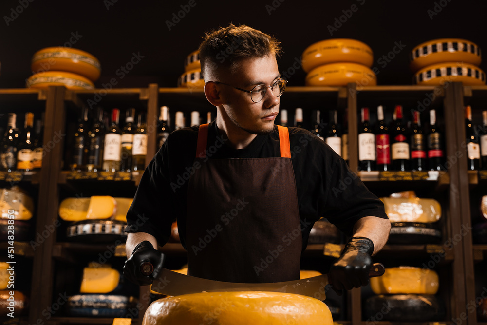 Cheese sommelier cutting yellow cheese wheel cut in half with a knife ...