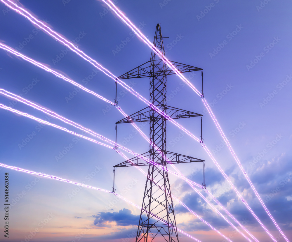 Electric transmission tower with glowing wires against the sunset sky ...