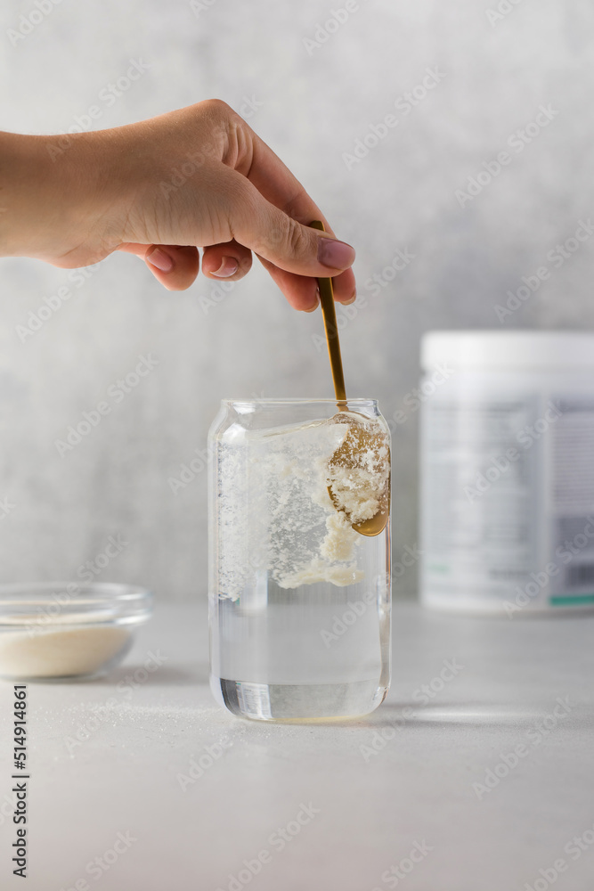 Hydrolyzed collagen powder is added with a spoon to a transparent glass ...