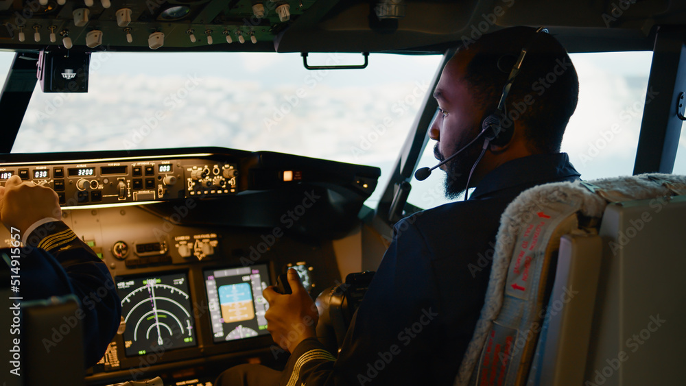 African american copilot flying airplane with captain in cockpit ...