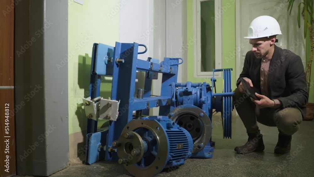 Technician, foreman in helmet and jacket unscrews nut on new electric motor before installation ...