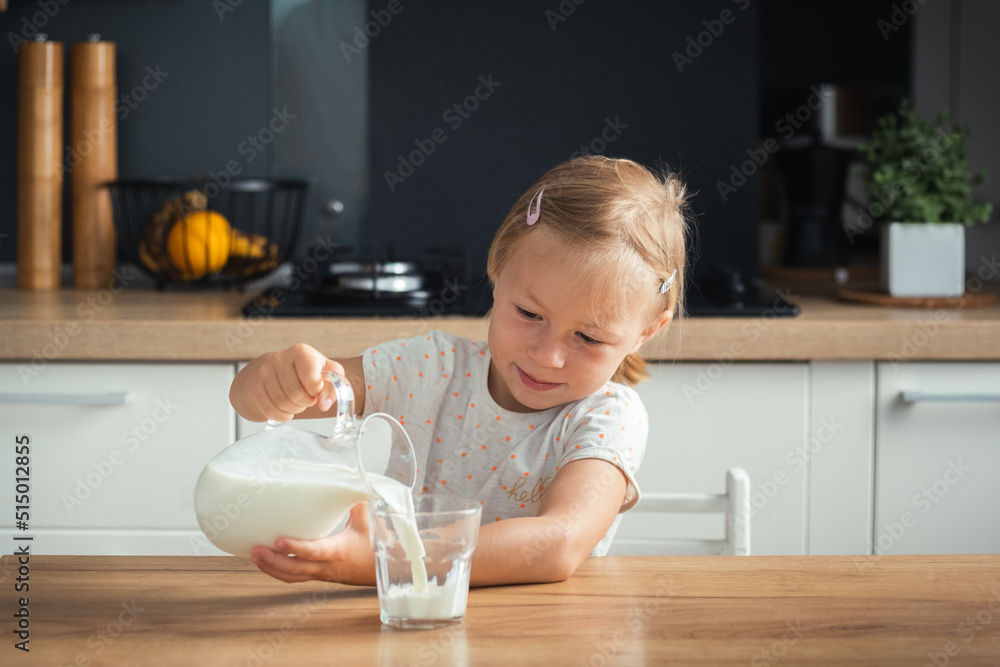 Happy little caucasian girl pouring milk in the glass in the stylish ...