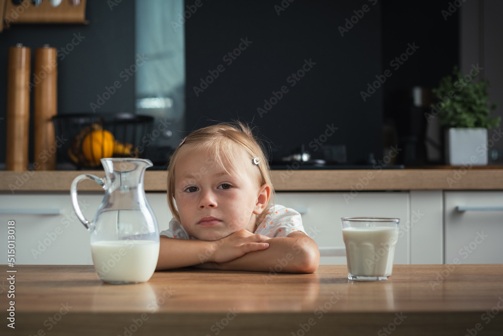 Sad little caucasian girl refuses to drink milk in the stylish kitchen ...