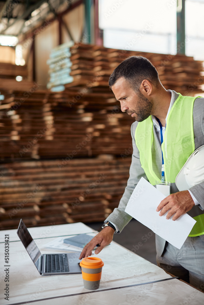 Wood warehouse owner workr on laptop while going through paperwork ...