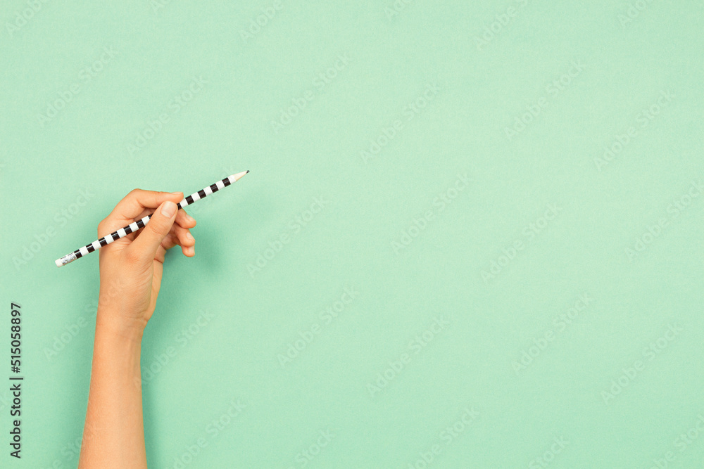 Left hand holding pencil for writing over light green background. Left ...
