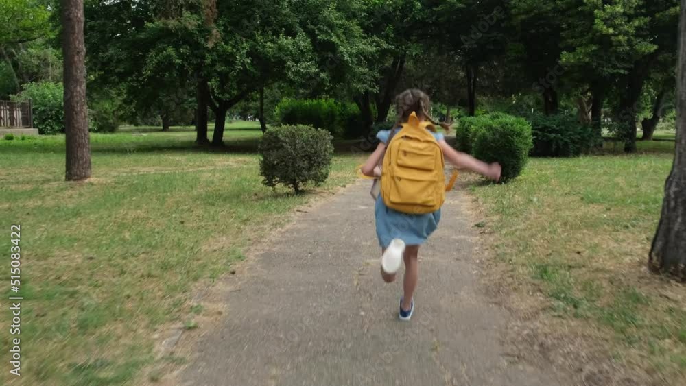 Little schoolgirl with school backpack and book runs through the park ...