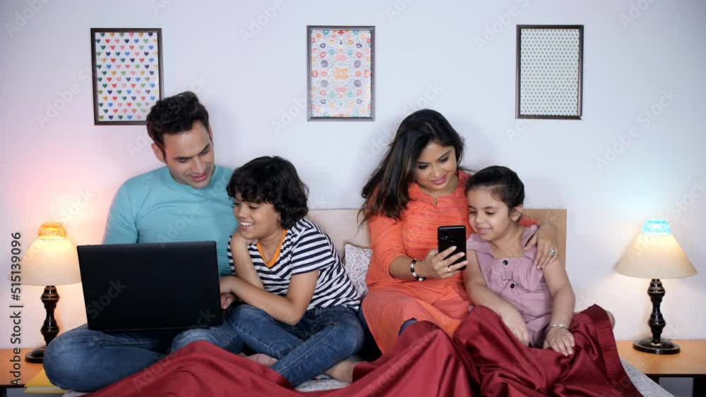A cheerful Indian family busy using digital gadgets in their free time ...