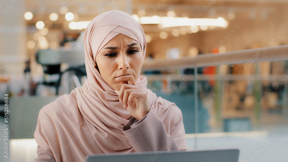 Young pensive puzzled arab woman in hijab working on laptop ...