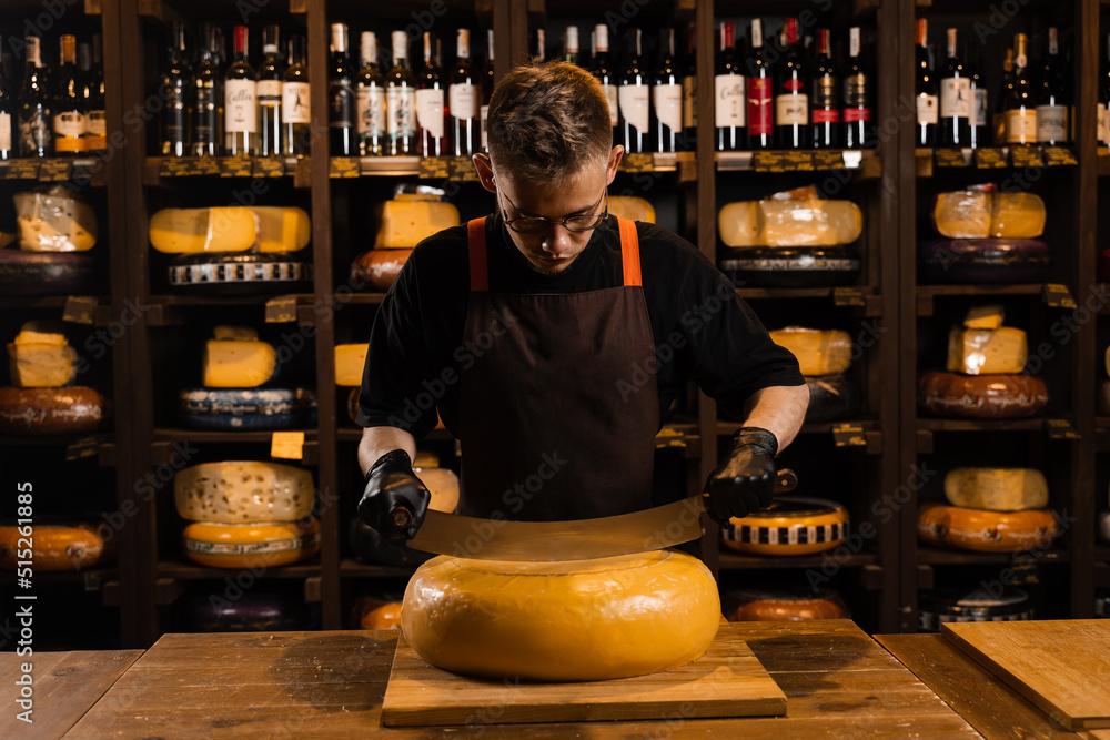 Cheese sommelier cutting yellow cheese wheel cut in half with a knife ...