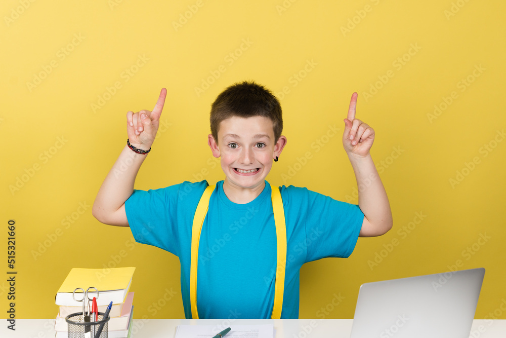 Cute schoolboy pointing up to copy space isolated on yellow background ...