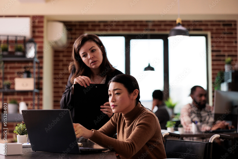 Asian woman with physical impairment brainstorming ideas with manager, paralyzed wheelchair user ...