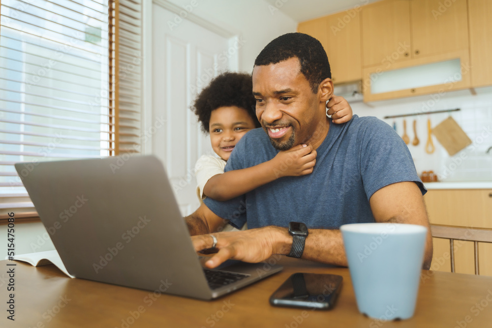 African American father working on laptop while his son distracts him ...
