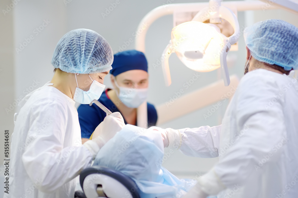 Surgeons and nurse during a dental operation. Anesthetized patient in ...