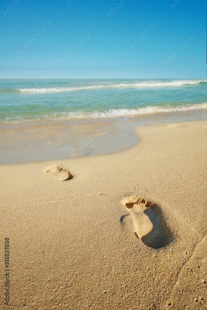 Footsteps on a sand beach seaside with a white foamy wave from the blue ...
