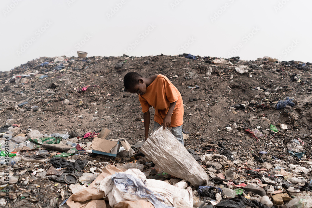 Street boy filling a plastic bag with reusable items found at a ...