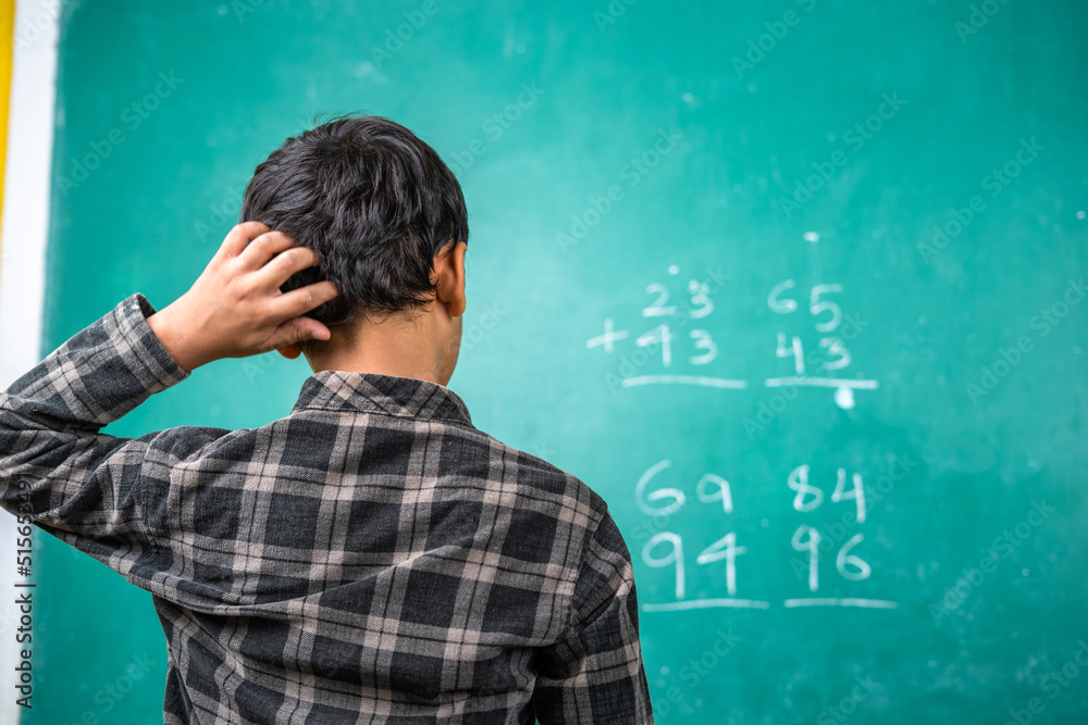 Confused kid scratching head to solve mathematics problem on board at ...