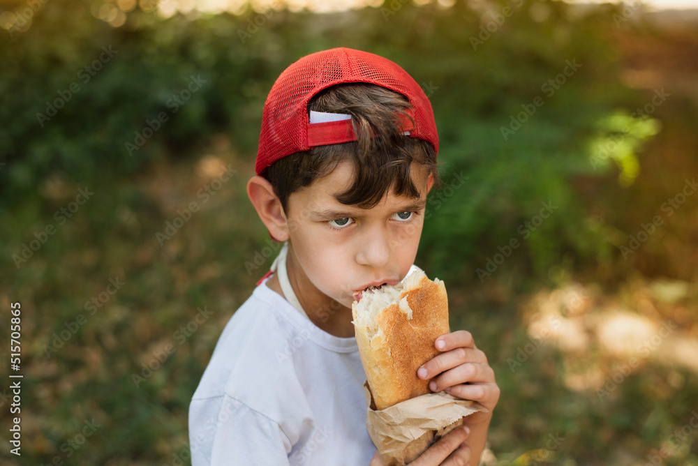 A young boy is very hungry and with a sad look eats a loaf of white ...