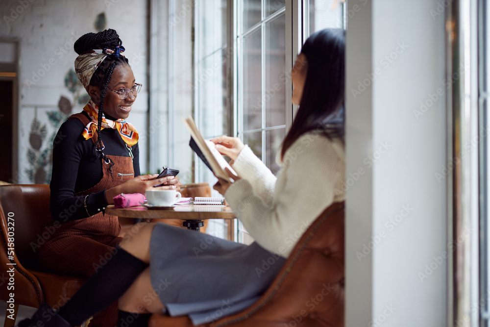 Two young multicultural women are sitting by the window in a cafe and ...