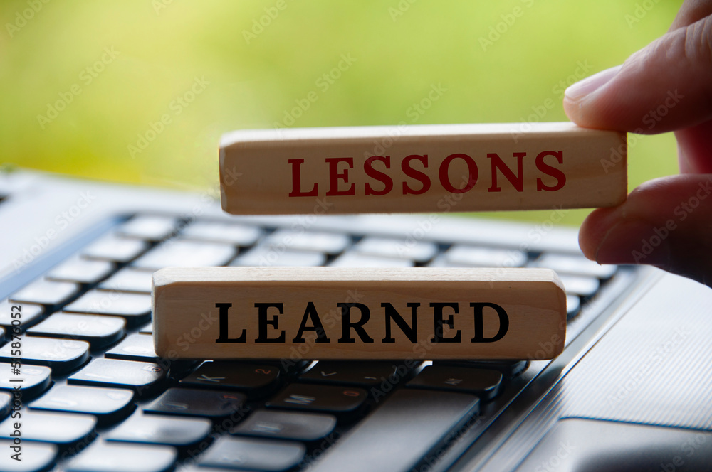 Hand holding lessons learned text on wooden blocks on top of a laptop ...