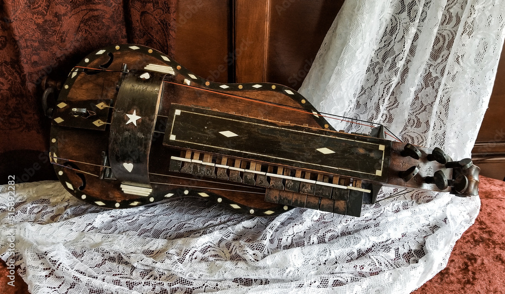 An antique musical instrument known as a Hurdy-Gurdy shown on a lace ...