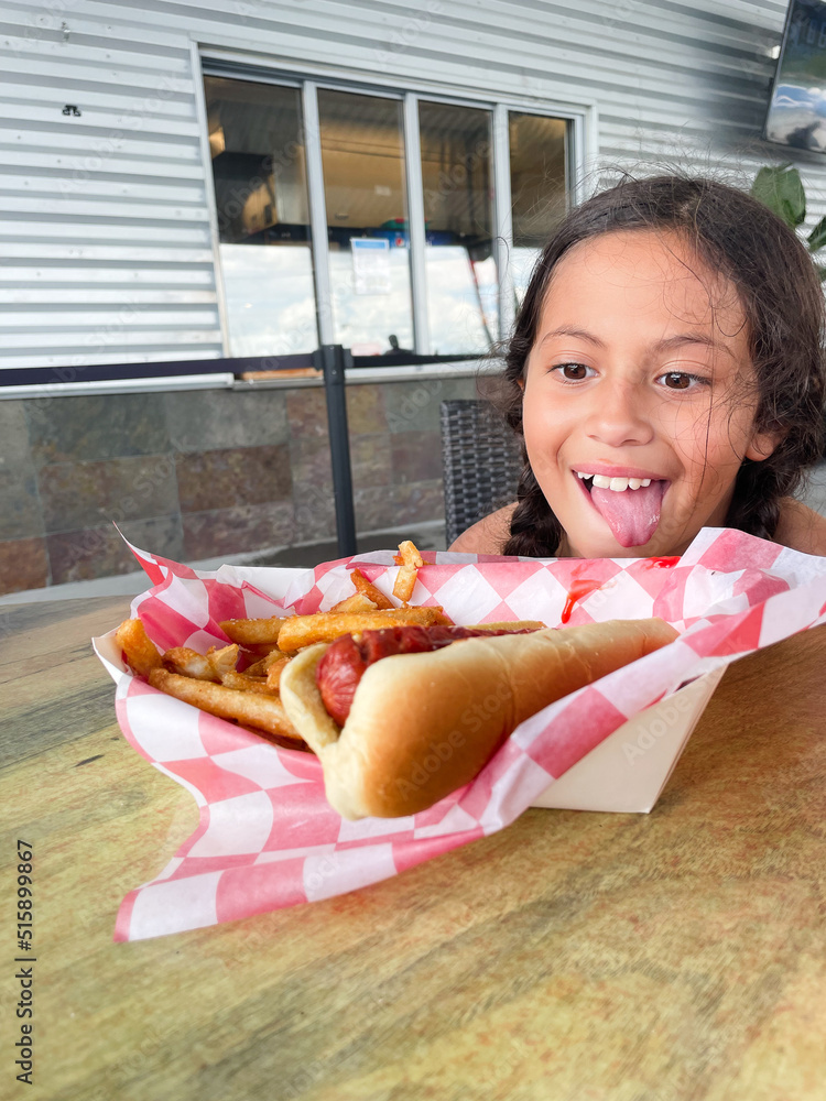 young girl sitting and staring hungrily at fresh hot dog and fries with ...