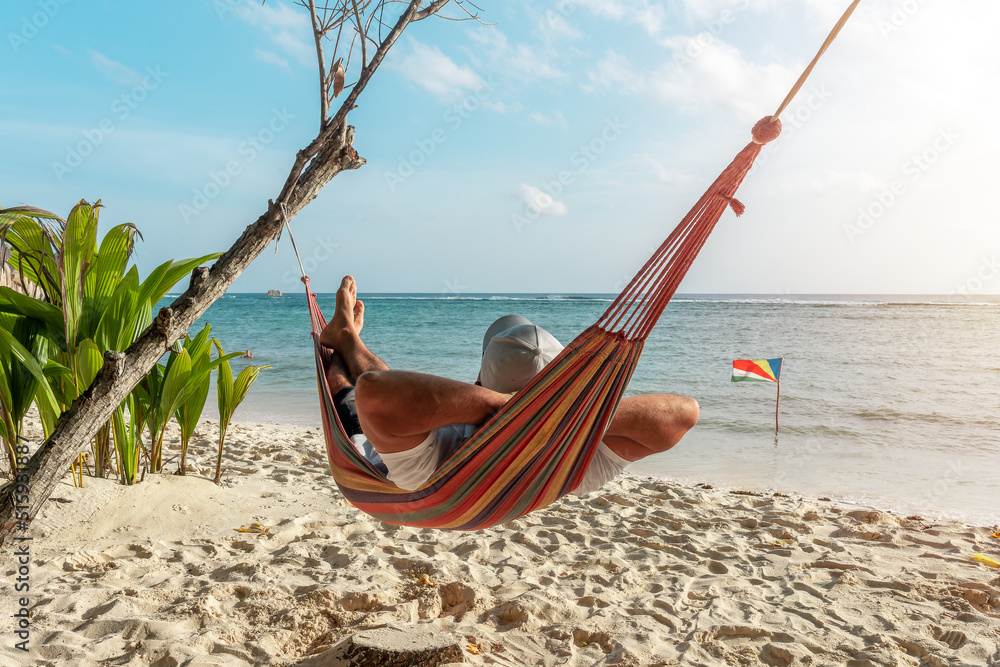Tourist relaxing in a hammock on a tropical beach overlooking the ...