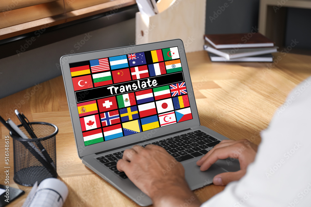 Translator using modern laptop with images of different flags on screen ...
