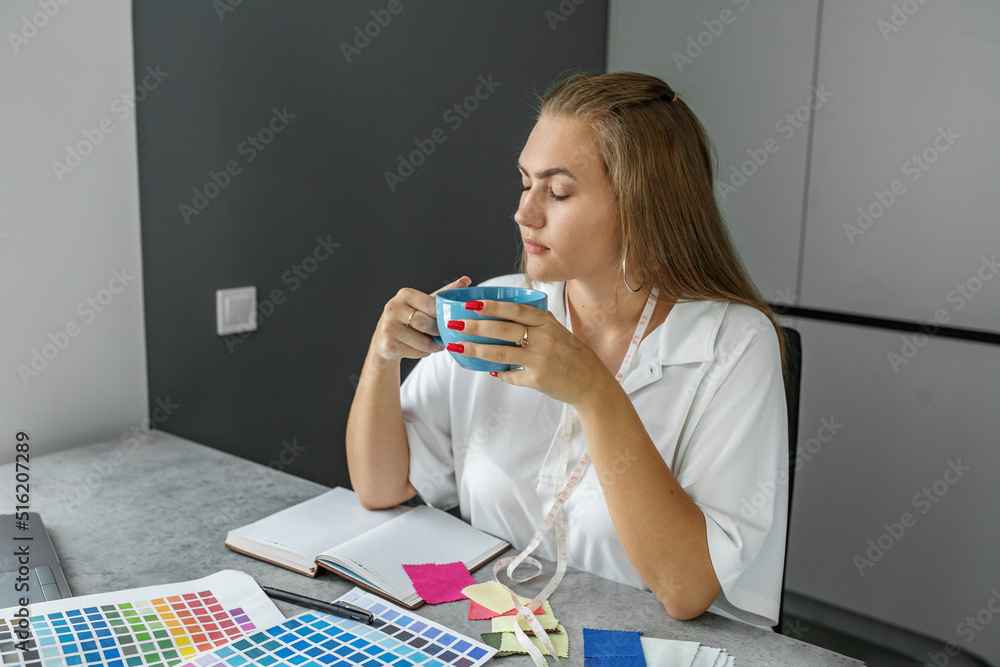 Woman sits at table in modern office next to color palette and fabric ...