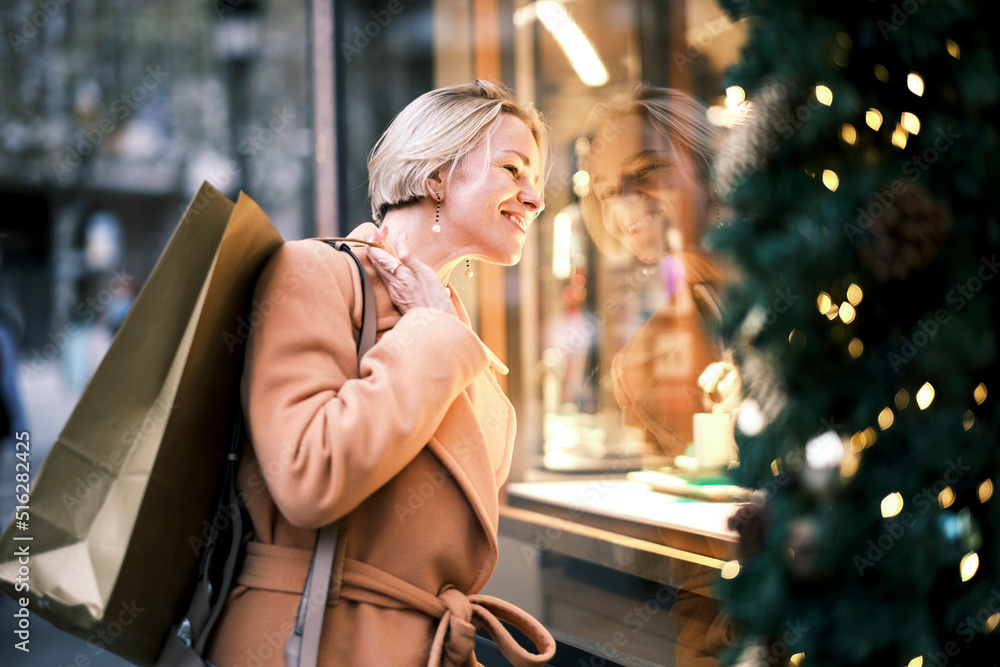 Beautiful woman with shopping bag looking through window of store Stock ...