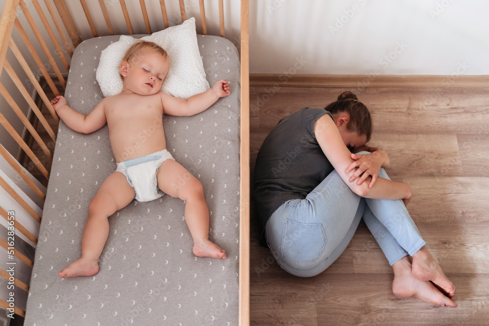 Upper view of cute baby napping in his bed next to his mother lying on ...