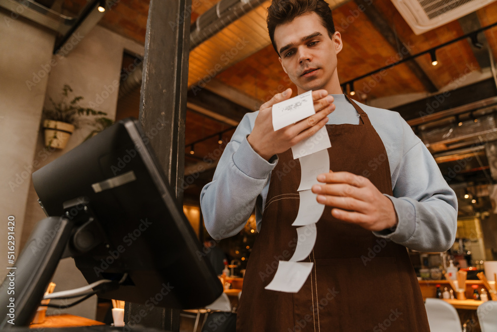 Young waiter man standing in front of computer and holding receipt ...