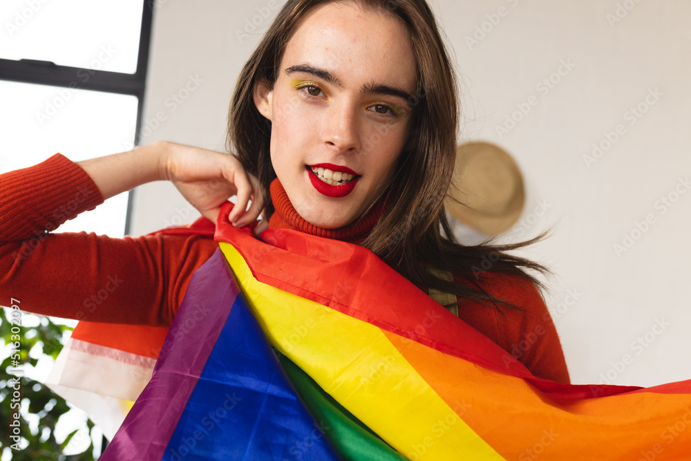 Image of happy caucasian non-binary trans woman holding rainbow fabric ...