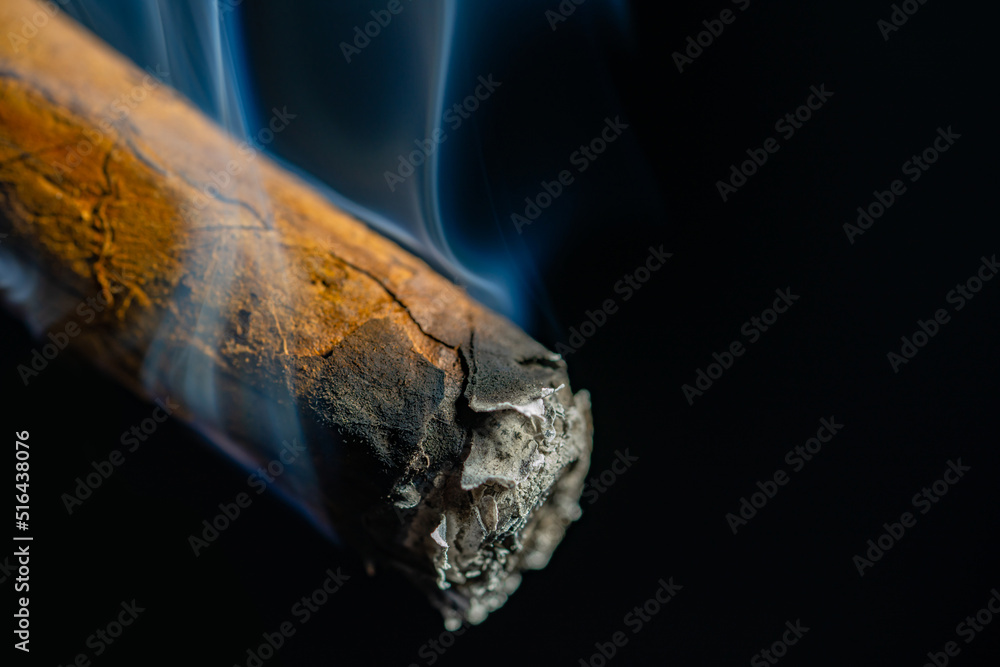 Smoking cuban cigar with blue smoke on an isolated black background. A ...