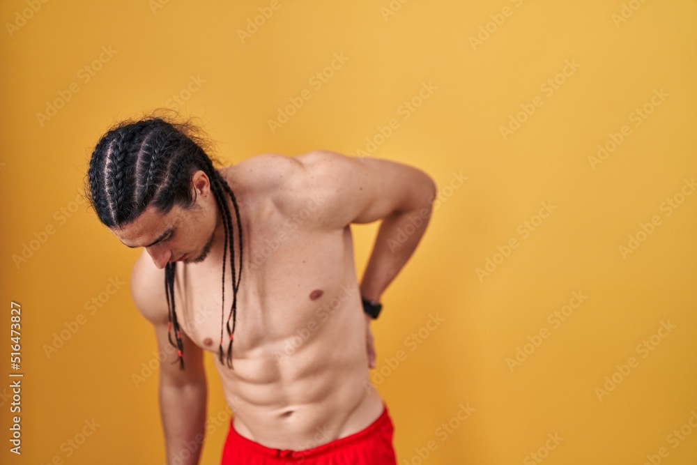 Hispanic man with long hair standing shirtless over yellow background ...