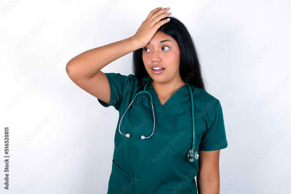 Doctor hispanic woman wearing surgeon uniform over white wall surprised ...