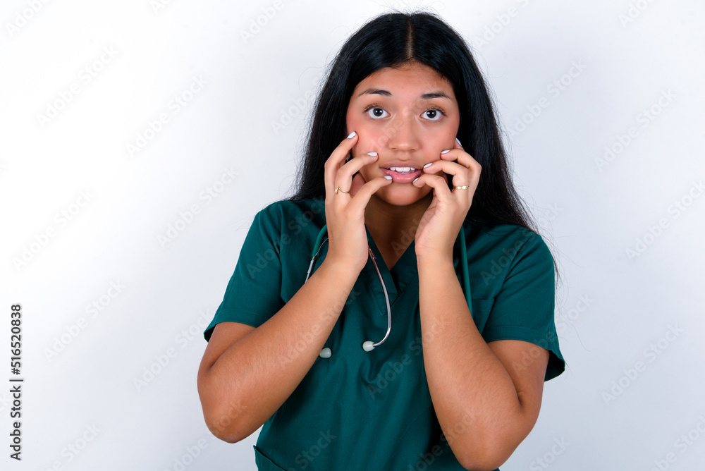 Stupefied Doctor hispanic woman wearing surgeon uniform over white wall ...