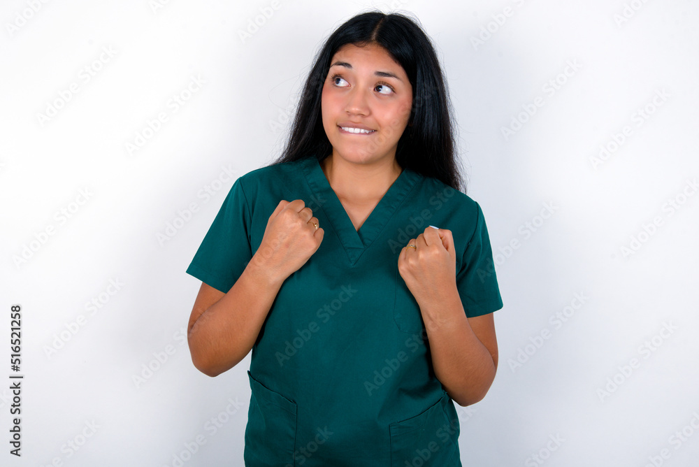 Doctor hispanic woman wearing surgeon uniform over white wall clenches ...