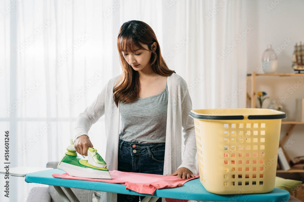 elegant asian young wife is pressing the clothes with concentration ...