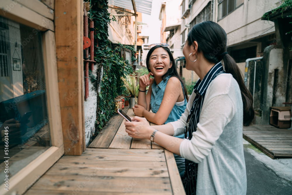 two cheerful Asian sister besties are laughing while using phone and ...