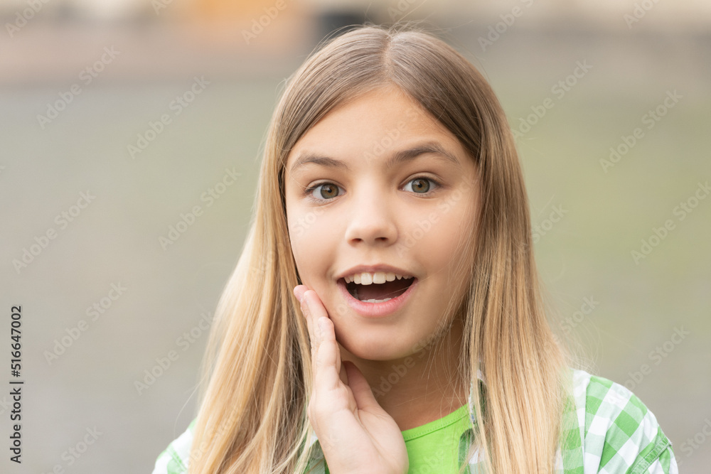 Portrait of tween girl with surprised face holding hand on cheek blurry ...